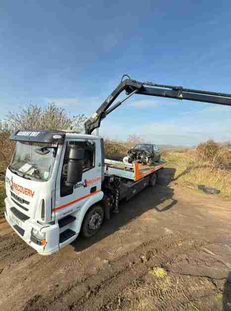 White Bath Recovery truck with crane arm lifting damaged vehicle in ...