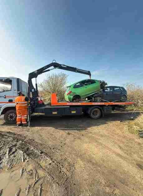 White Bath Recovery truck with crane lifting green damaged car in field